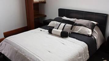 Cama bem arrumada com cabeceira preta, roupa de cama listrada em preto e branco e almofada bege.