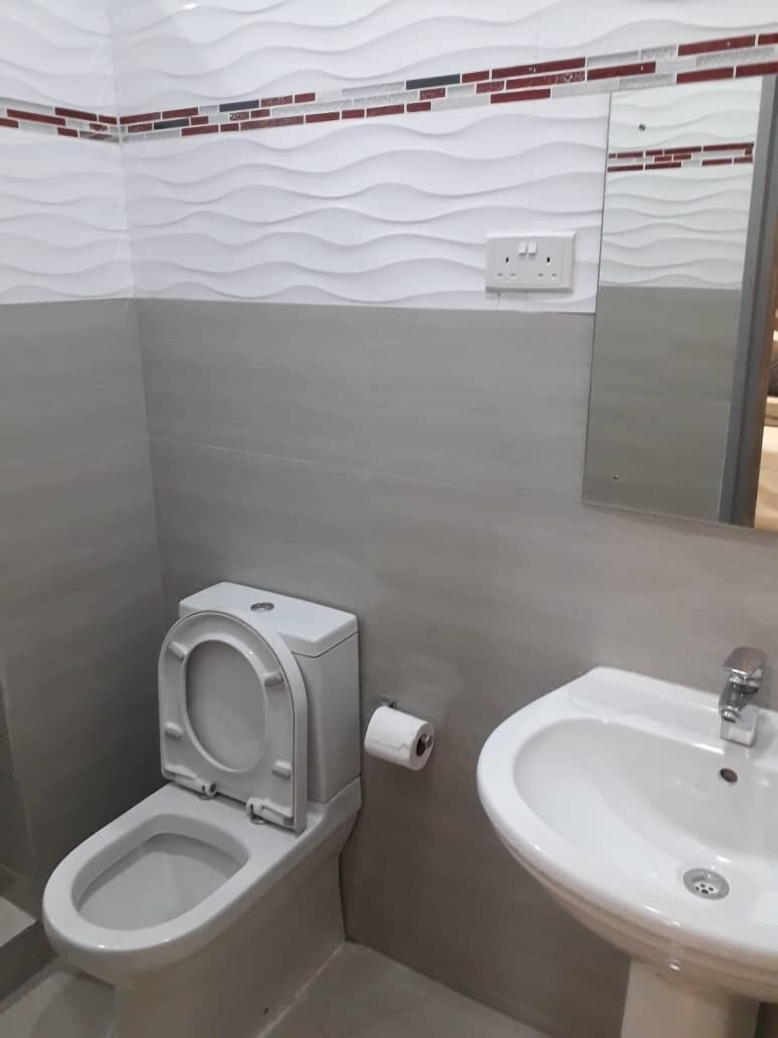 Uma casa de banho moderna com sanita, lavatório e paredes em azulejo.