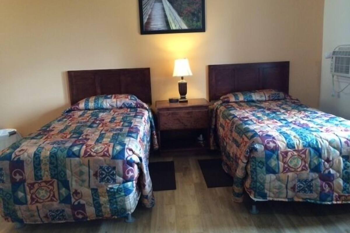 Quarto com duas camas, cada uma com um colcha colorida, uma mesa de cabeceira com luminária e um quadro na parede.