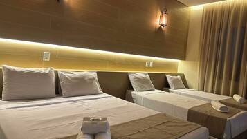 Quarto de hotel com duas camas, cabeceira, luminárias fixadas na parede e cortina.
