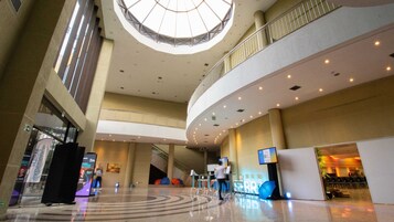 Um hall amplo com teto alto, um átrio central e uma escadaria em curva.