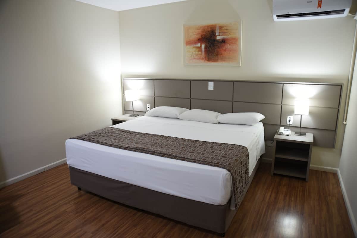 Uma cama bem arrumada com um cobertor marrom, duas mesas de cabeceira com abajures e um ar-condicionado fixado na parede.