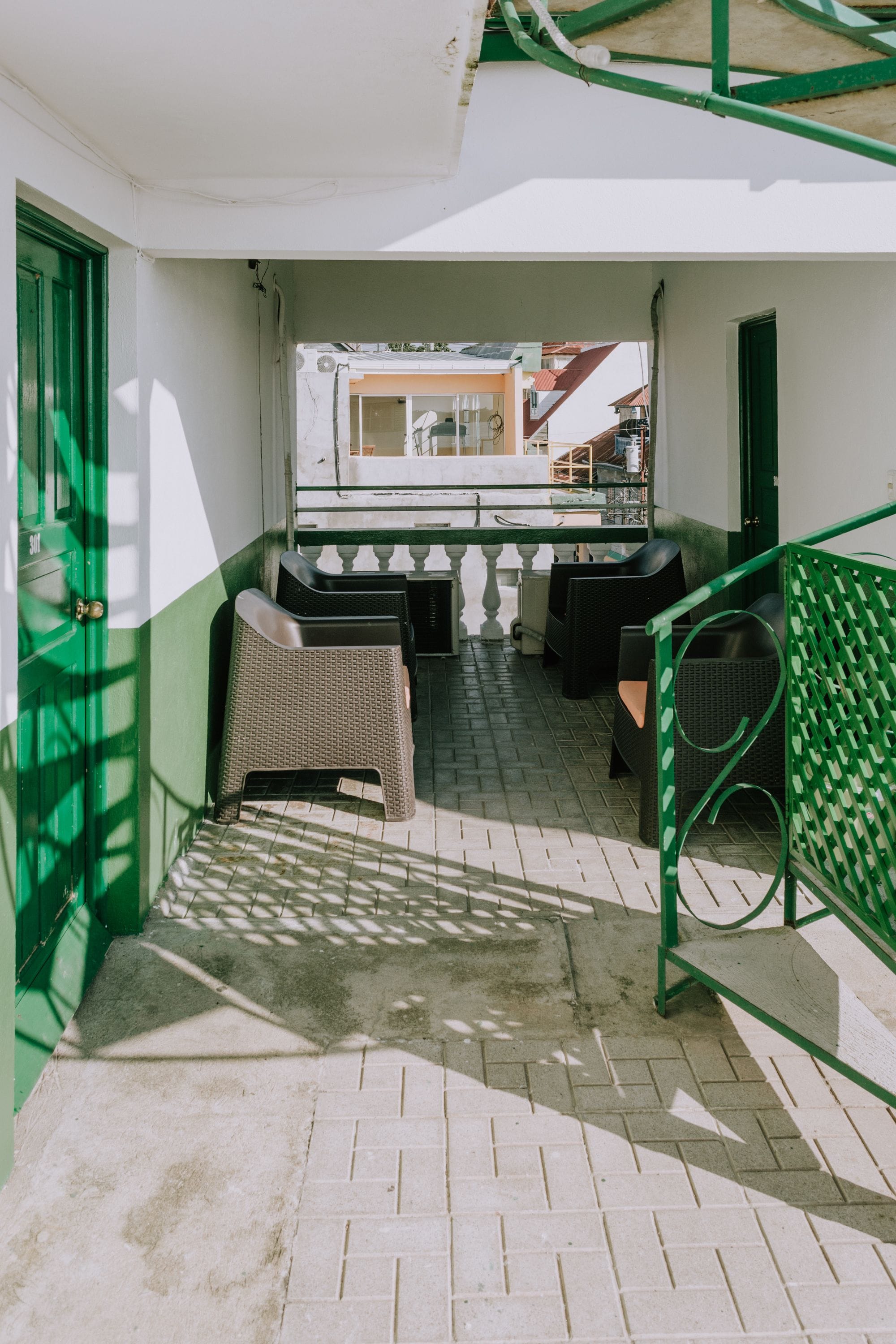Uma varanda com móveis de vime, grade de metal verde e vista para edifícios vizinhos.