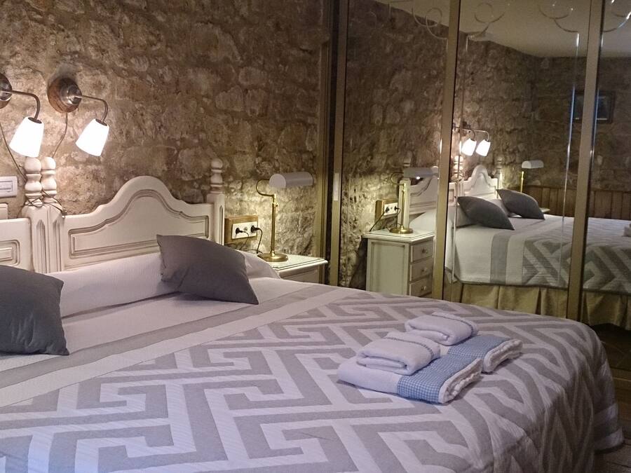 Quarto com uma cama grande, um espelho e uma parede de pedra.