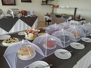 Disposição de buffet com recipientes de comida tampados, pratos e utensílios.