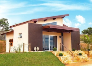 Uma casa moderna de dois andares com telhado plano, grandes portas de vidro e uma escadaria de pedra que dá acesso à entrada.