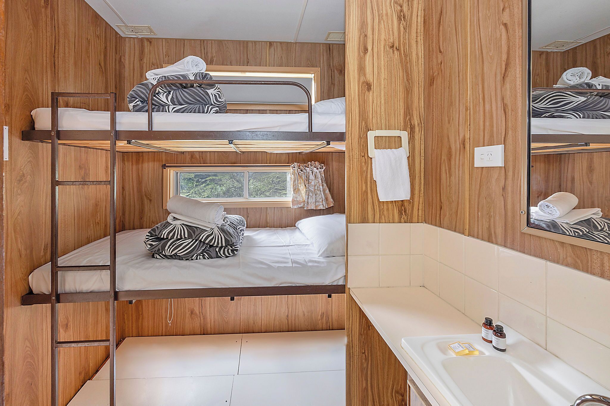 Quarto com beliche, janela, pia e espelho.