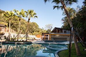 Uma piscina com design curvo, rodeada por palmeiras e um edifício com área coberta.