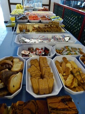 Mesa de buffet com diversos alimentos, incluindo pão, doces e acompanhamentos.