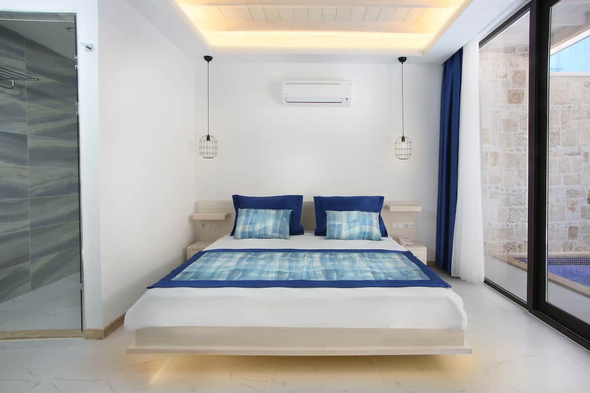 Quarto moderno com cama, mesas de cabeceira e vista para uma parede de pedra e piscina através de uma porta de vidro.