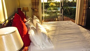 Quarto de hotel com cama, mesa e vista para a piscina e jardim.
