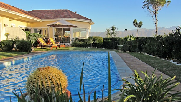 Piscina com área de estar, rodeada por vegetação e vista para montanhas.