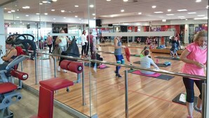Uma academia com equipamentos de ginástica, espelhos e pessoas se exercitando.