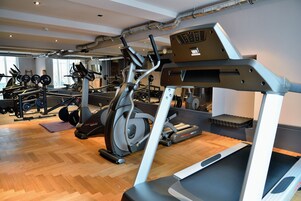 Uma academia com equipamentos de cardio, aparelhos de musculação e um espelho grande na parede.