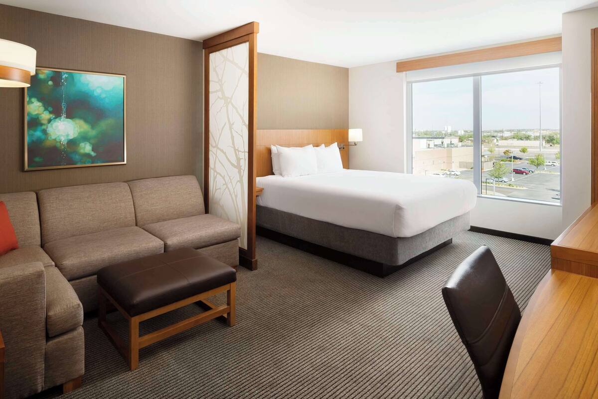 Quarto de hotel com sofá, cama, escrivaninha e uma janela grande com vista para a cidade.