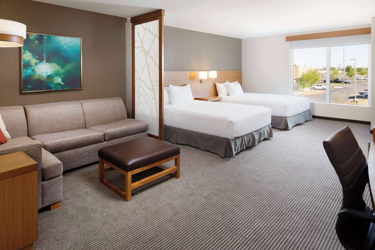 Quarto de hotel com sofá, duas camas, escrivaninha e vista para o estacionamento.