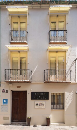 Um edifício com uma placa indicando 'LA SIESTA DE PICASSO', varandas com grades de metal e uma porta de madeira.