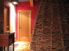 Um quarto com porta de madeira, uma mesinha com abajur e uma grande estrutura de fibra vegetal.