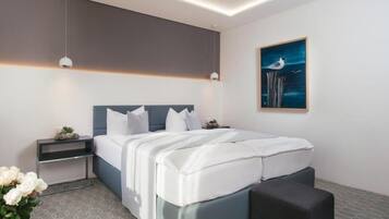 Quarto de hotel moderno com cama, mesas de cabeceira, uma pequena planta e um quadro na parede.