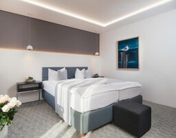 Quarto de hotel moderno com cama, mesas de cabeceira, uma pequena planta e um quadro na parede.