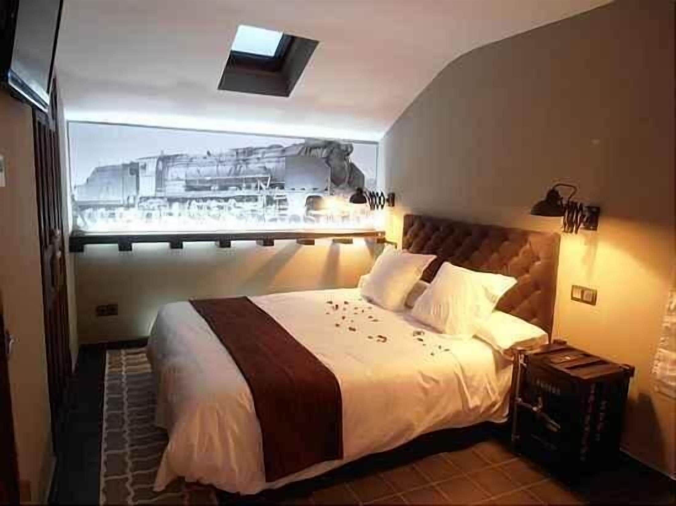 Quarto de hotel com cama, mesa de cabeceira, mala e janela com vista para a cidade.