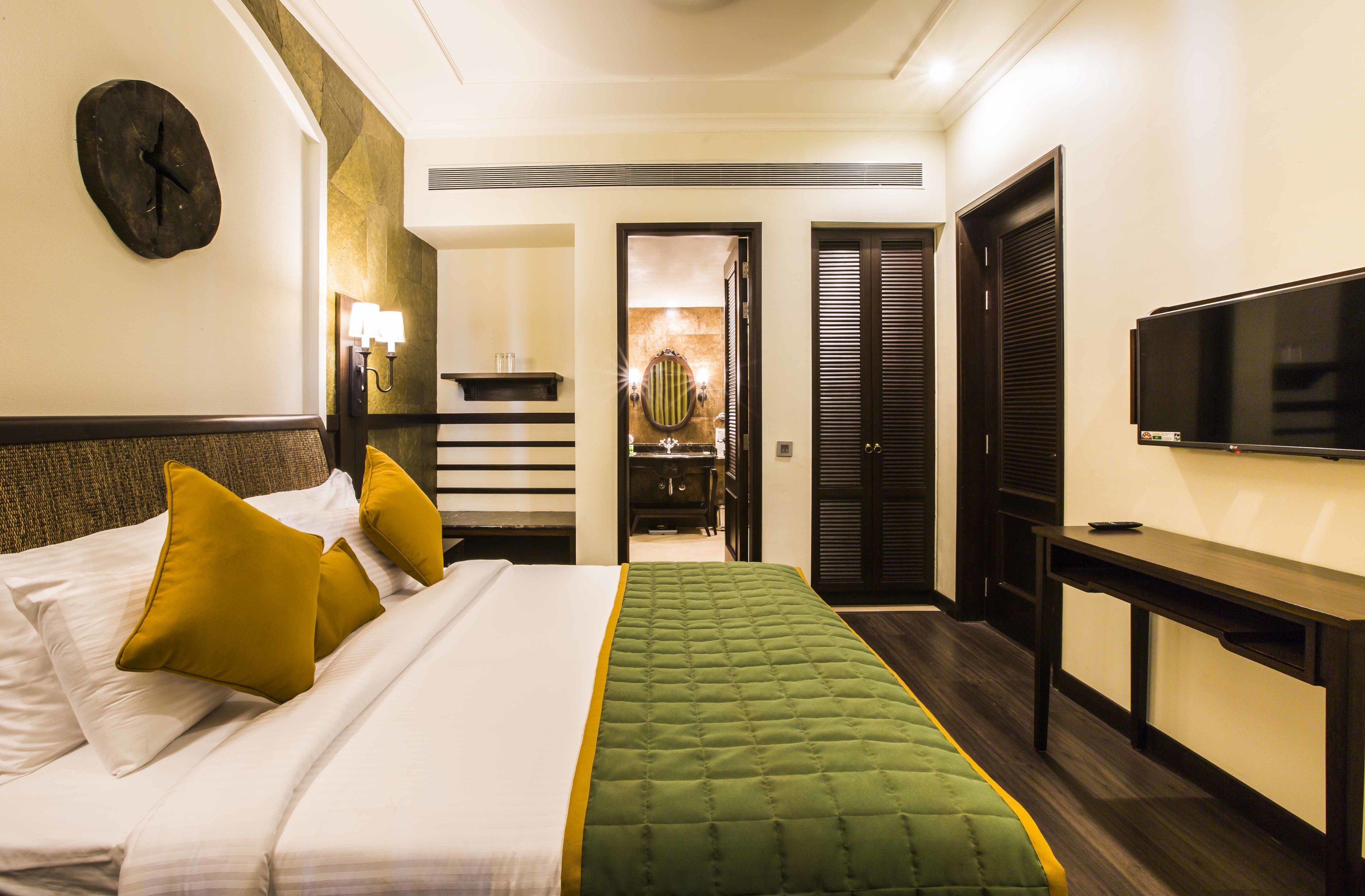 Quarto de hotel com cama, televisão, escrivaninha e espelho.