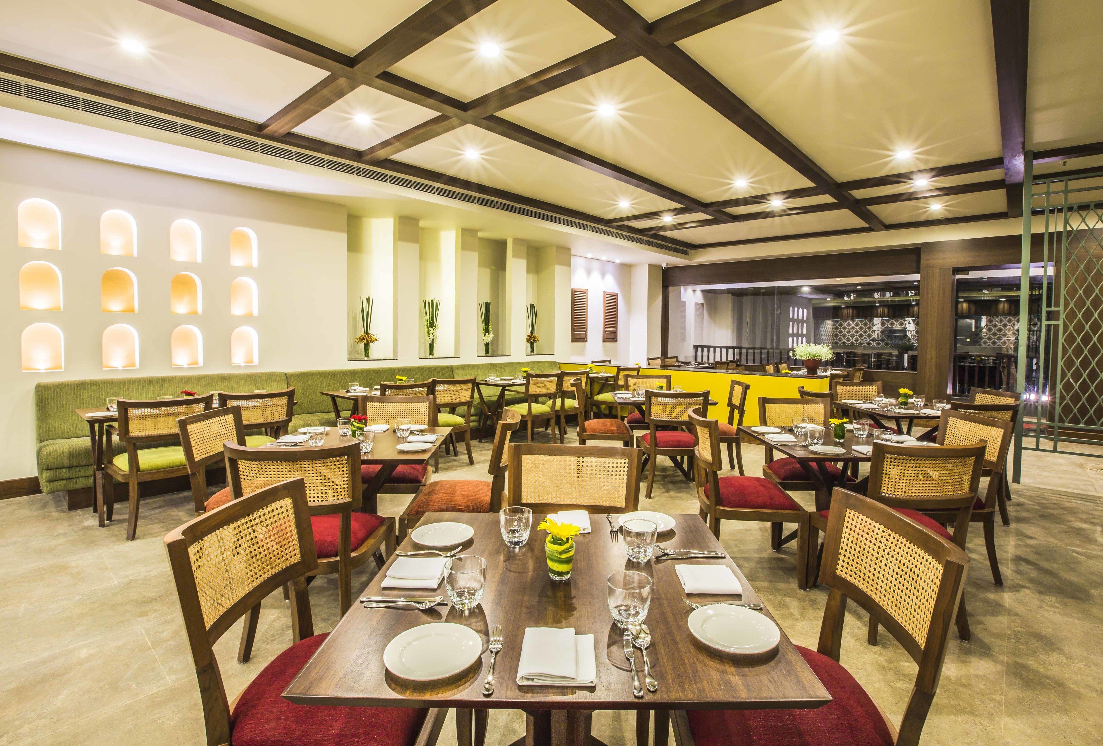 Um restaurante com mesas e cadeiras de madeira, um sofá verde e um balcão amarelo.