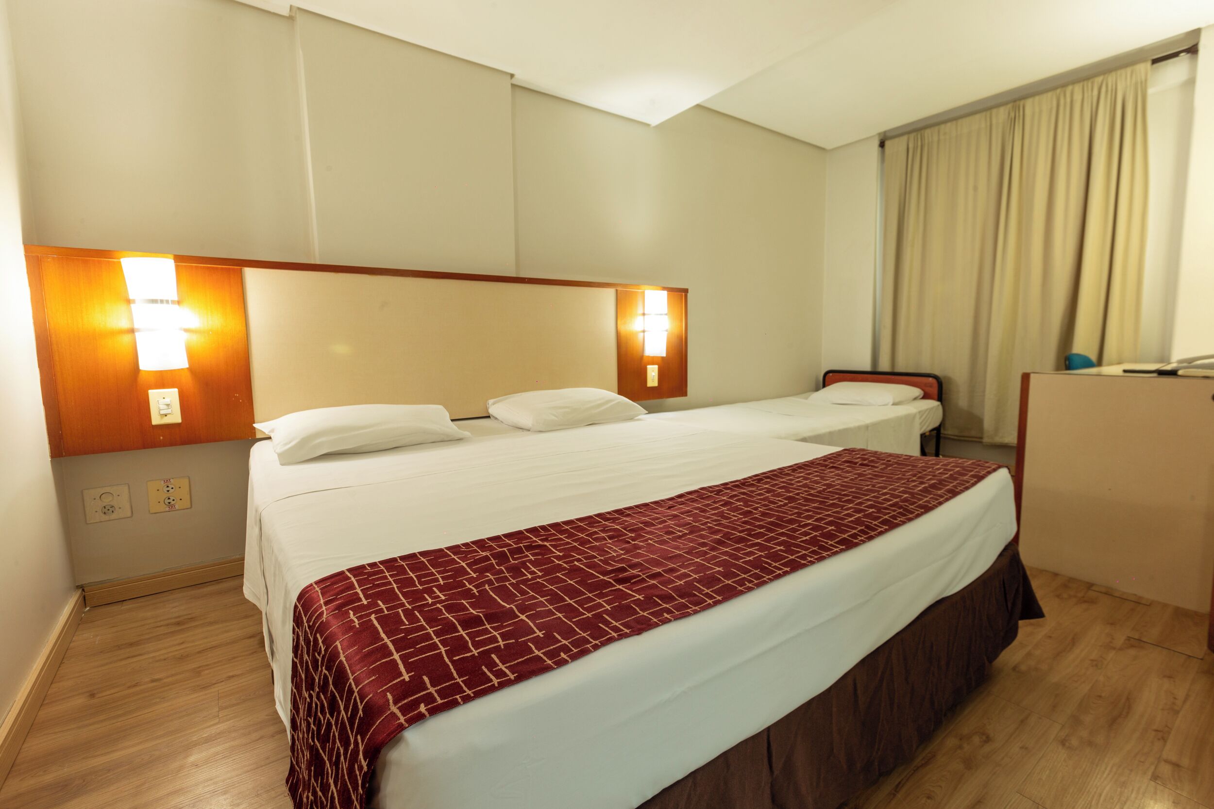 Quarto de hotel com uma cama grande, duas mesas de cabeceira, uma escrivaninha e um guarda-roupa.