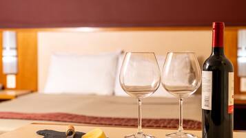 Quarto de hotel com cama, duas taças de vinho, uma garrafa de vinho e uma tábua de queijos sobre uma mesa.