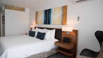 Quarto de hotel com uma cama grande, duas luminárias de cabeceira, uma mesa de cabeceira de madeira, uma cadeira e ar-condicionado fixado na parede.