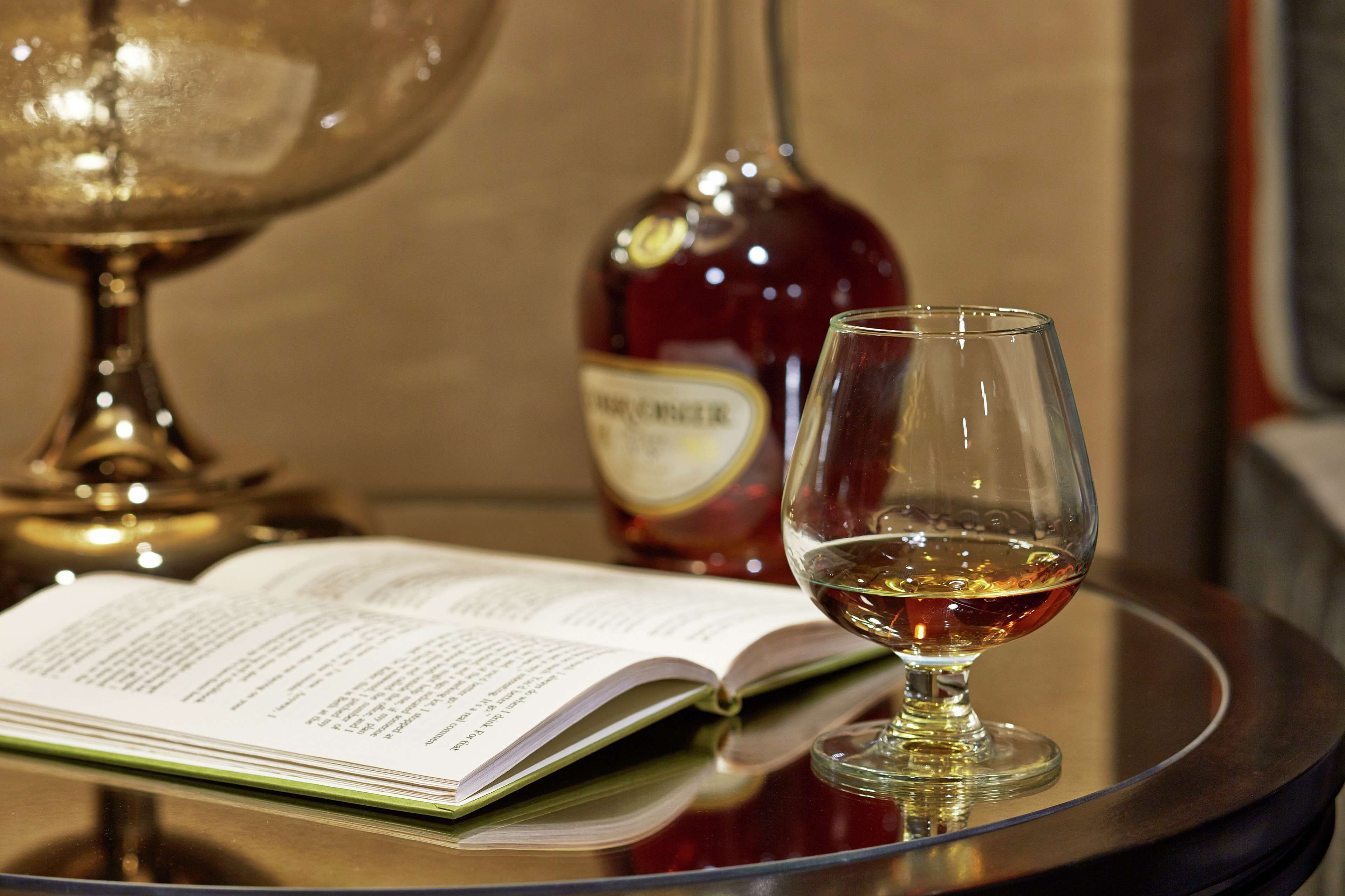 Um copo de vinho, uma garrafa e um livro aberto sobre uma superfície reflexiva.