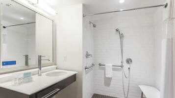 Uma casa de banho moderna com lavatório branco, espelho e chuveiro.