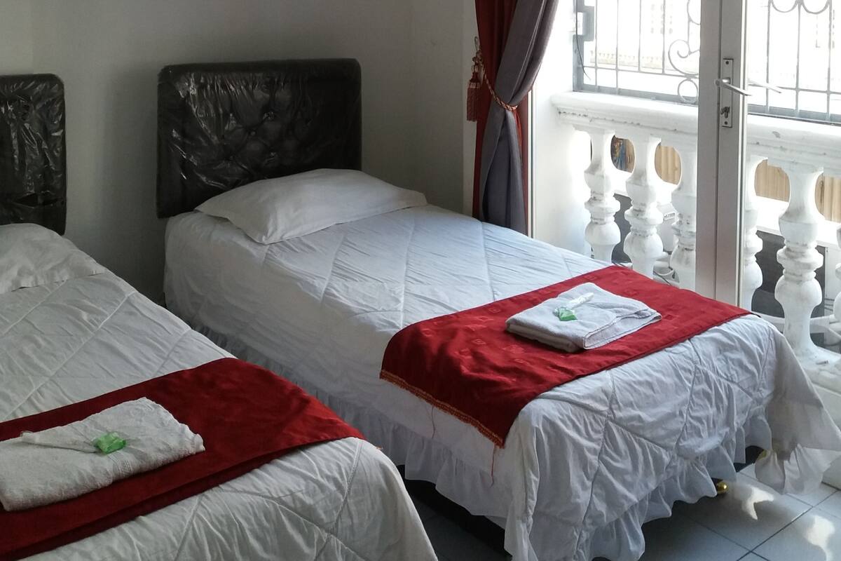 Quarto de hotel com duas camas, janela com grades de metal e teto branco.