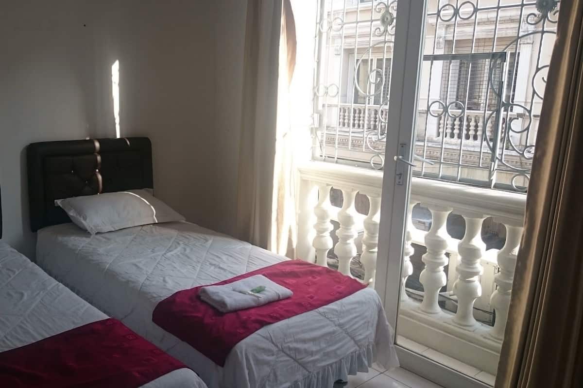 Quarto de hotel com duas camas, varanda com grade de ferro e vista para edifícios.