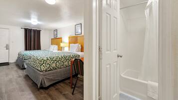 Quarto de hotel com cama, cadeira, mesa de cabeceira, luminária, cortina do chuveiro e porta.