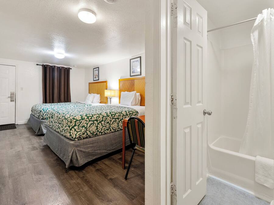 Quarto de hotel com cama, cadeira, mesa de cabeceira, luminária, cortina do chuveiro e porta.
