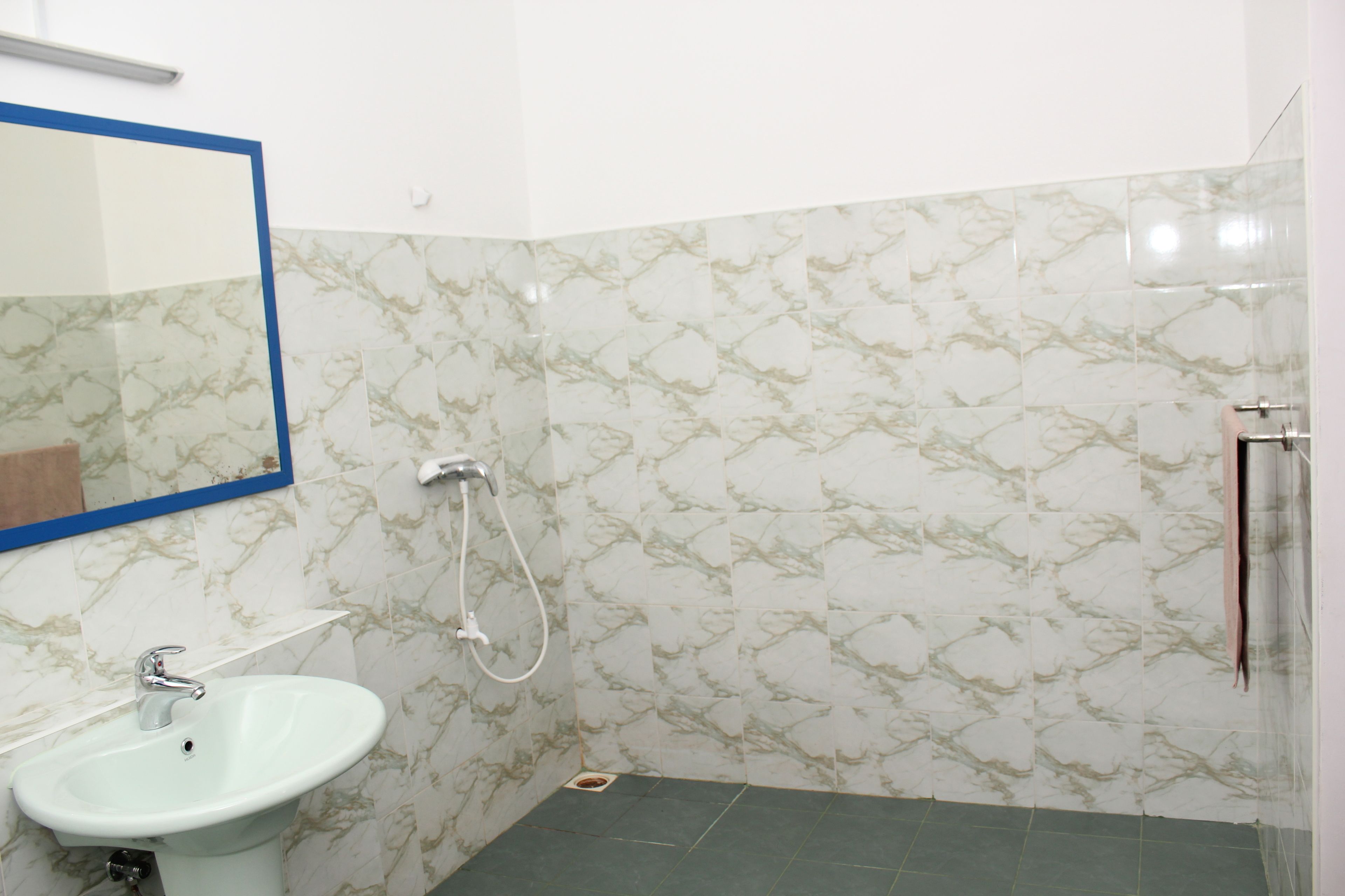 Casa de banho com lavatório branco, espelho e chuveiro com porta de vidro.