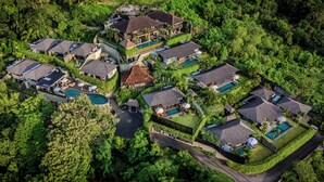 Vista aérea de um resort com vários edifícios, piscinas e vegetação exuberante.