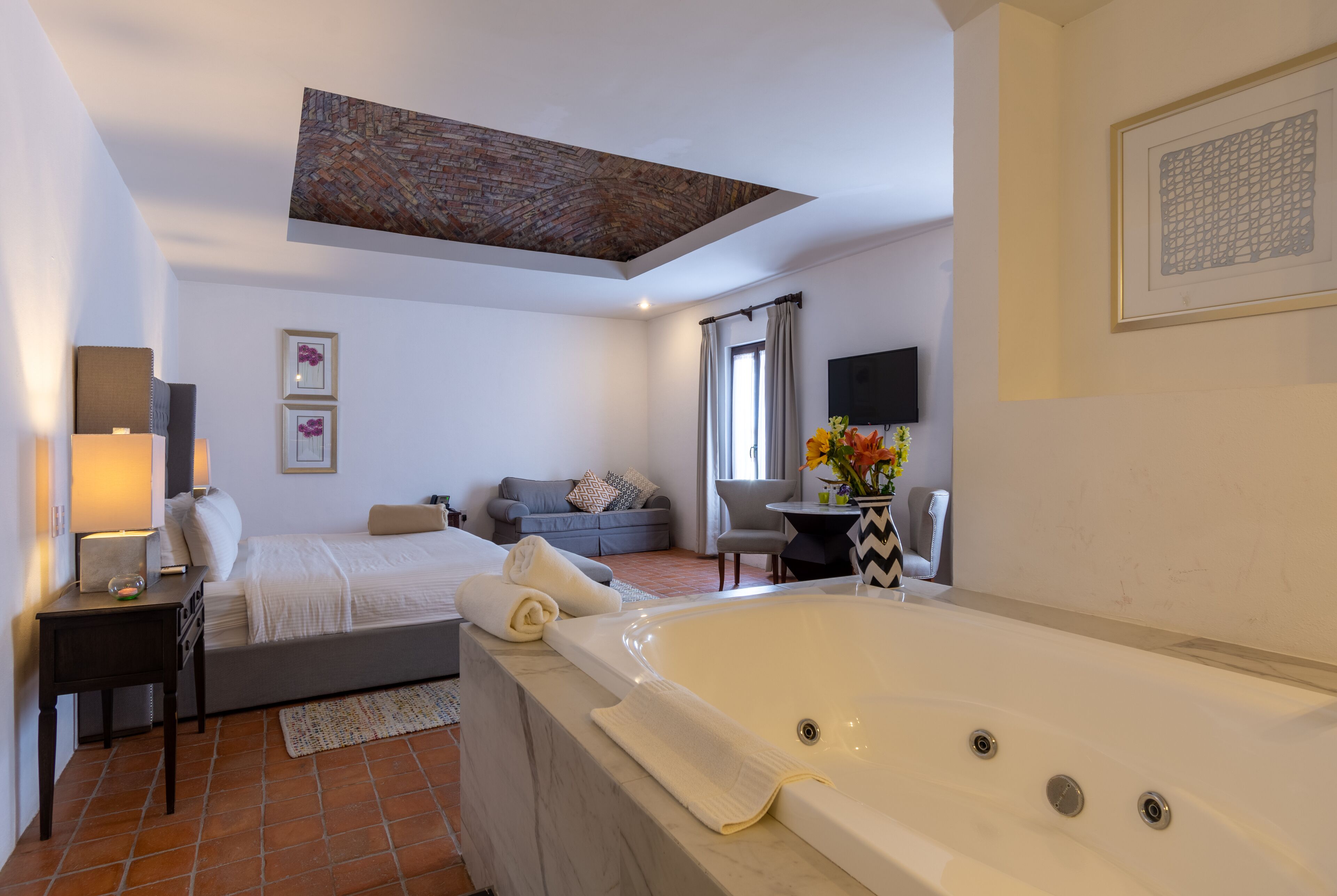 Quarto de hotel moderno com uma banheira grande, um sofá, uma mesa de jantar e uma TV.