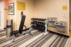 Academia de hotel com equipamentos de exercício, halteres, bebedouro e telefone.