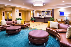 Um saguão de hotel com sofás de couro, uma mesa de recepção e um relógio na parede.