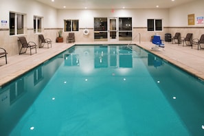 Uma grande piscina interior com água cristalina, rodeada por espreguiçadeiras e um elevador de piscina.
