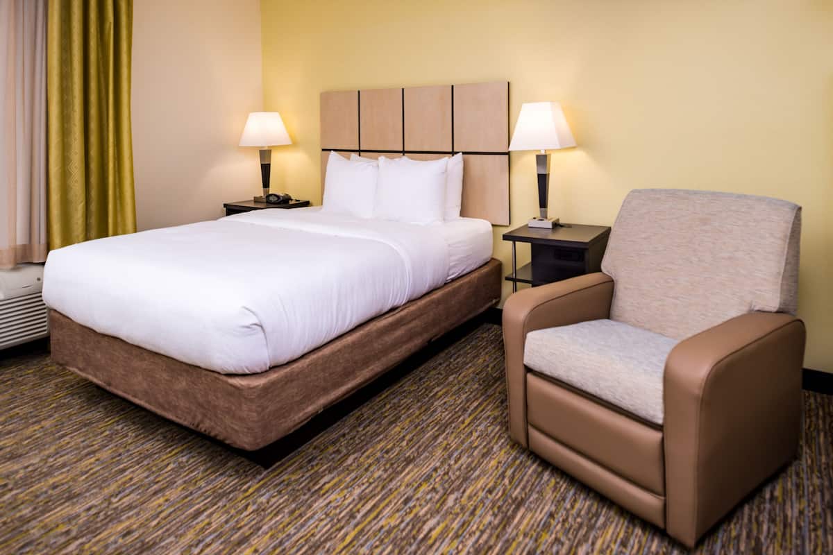 Quarto de hotel com uma cama grande, duas mesas de cabeceira com luminárias, uma cadeira e um tapete estampado.