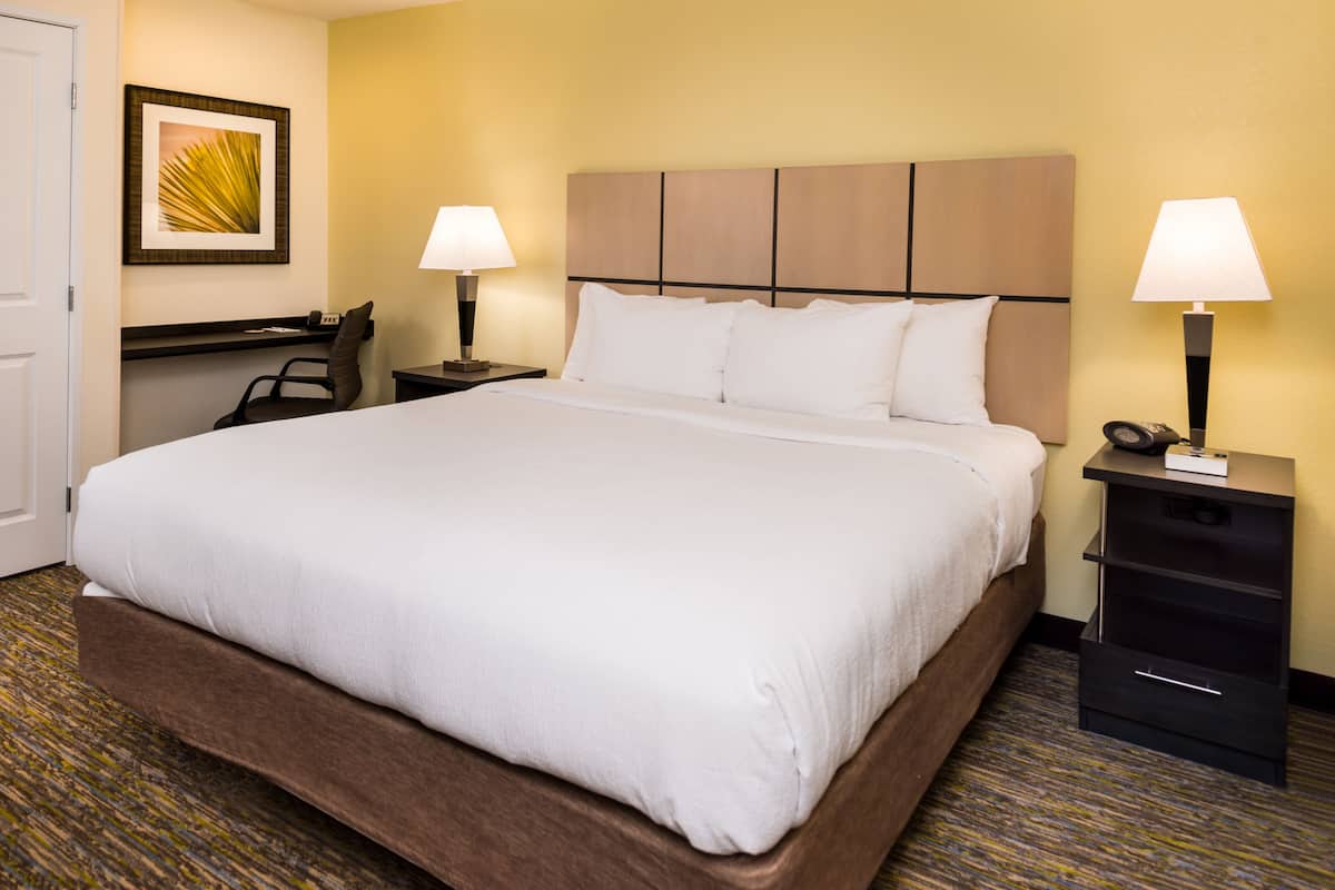 Quarto de hotel com uma cama grande, duas mesas de cabeceira com abajures, uma escrivaninha e uma cadeira.
