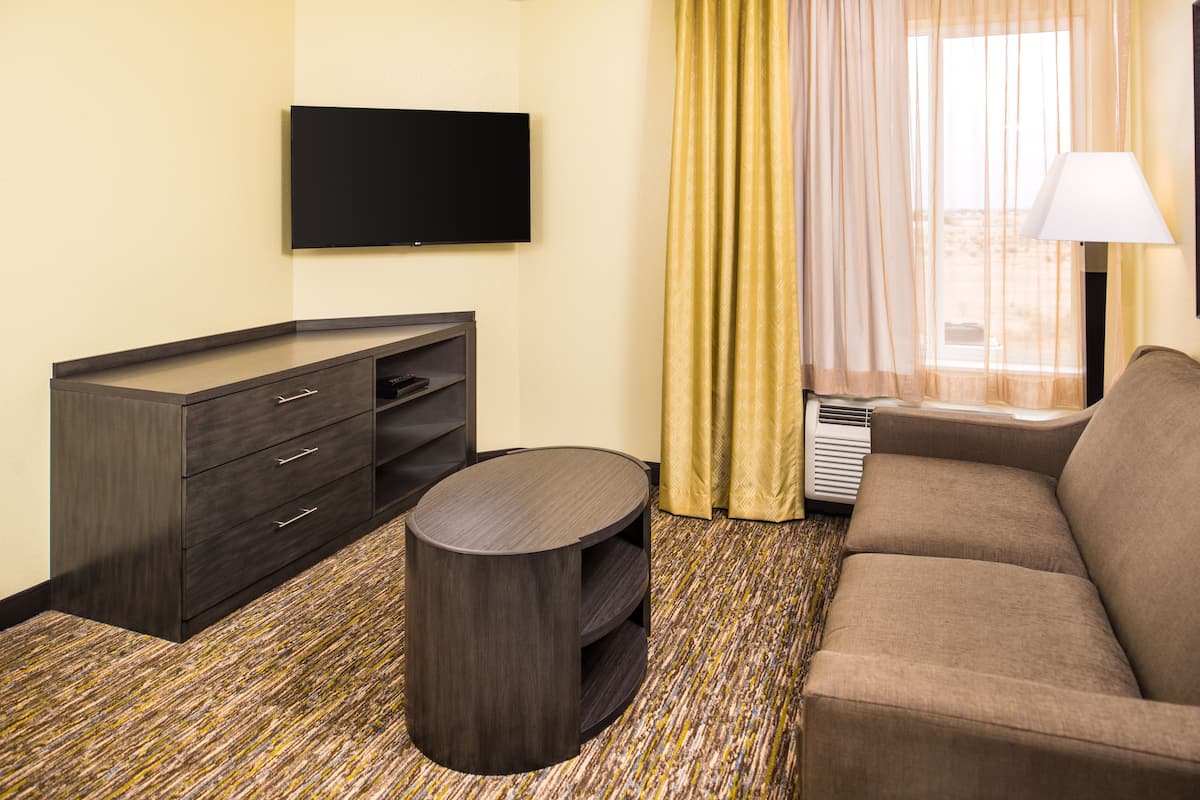Quarto de hotel com televisão de tela plana presa à parede, um sofá, uma mesa redonda pequena e um frigobar.