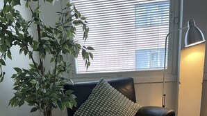 Quarto com poltrona de couro preta, planta em vaso, abajur e janela com persianas.