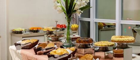 Uma mesa de buffet com diversos produtos de panificação e um vaso de flores brancas.