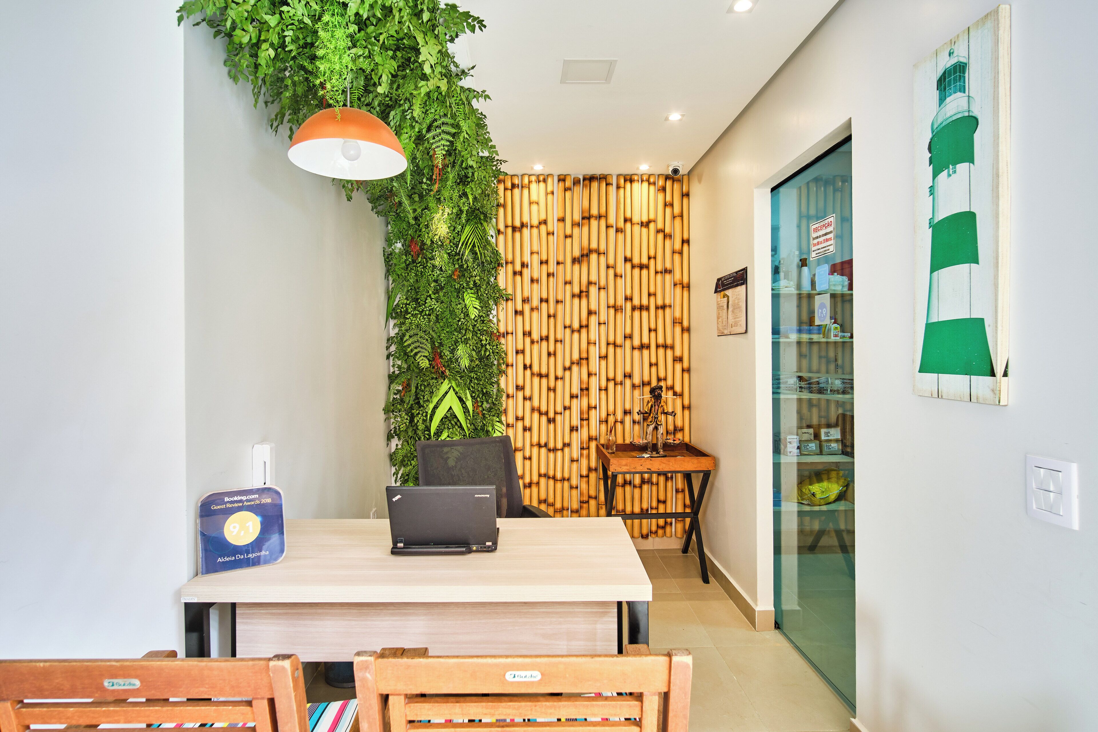 Quarto com parede de bambu, um laptop sobre uma mesa e uma porta de vidro com um objeto listrado em verde e branco.