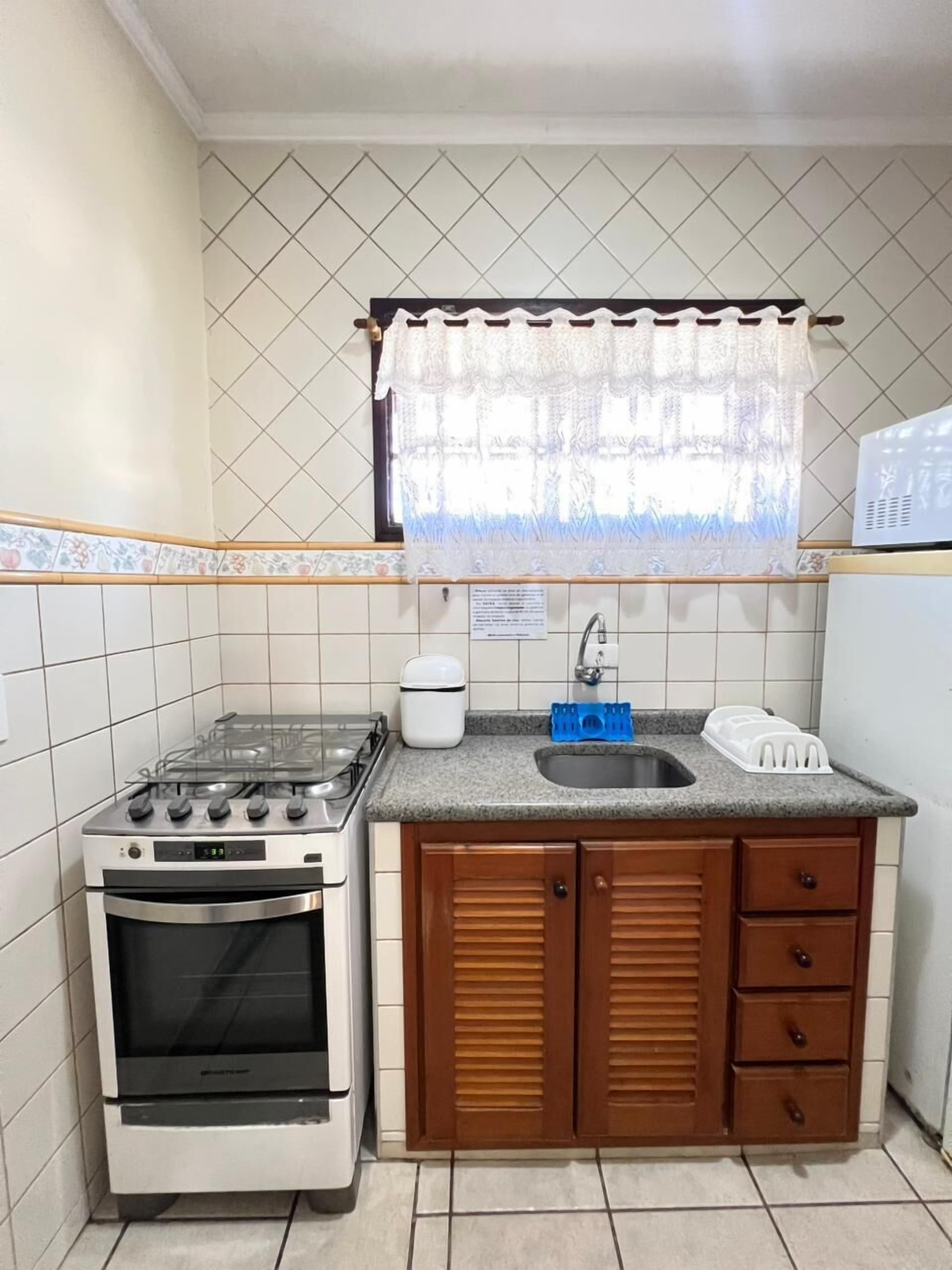 Cozinha compacta com fogão a gás, forno, pia e armários de madeira.
