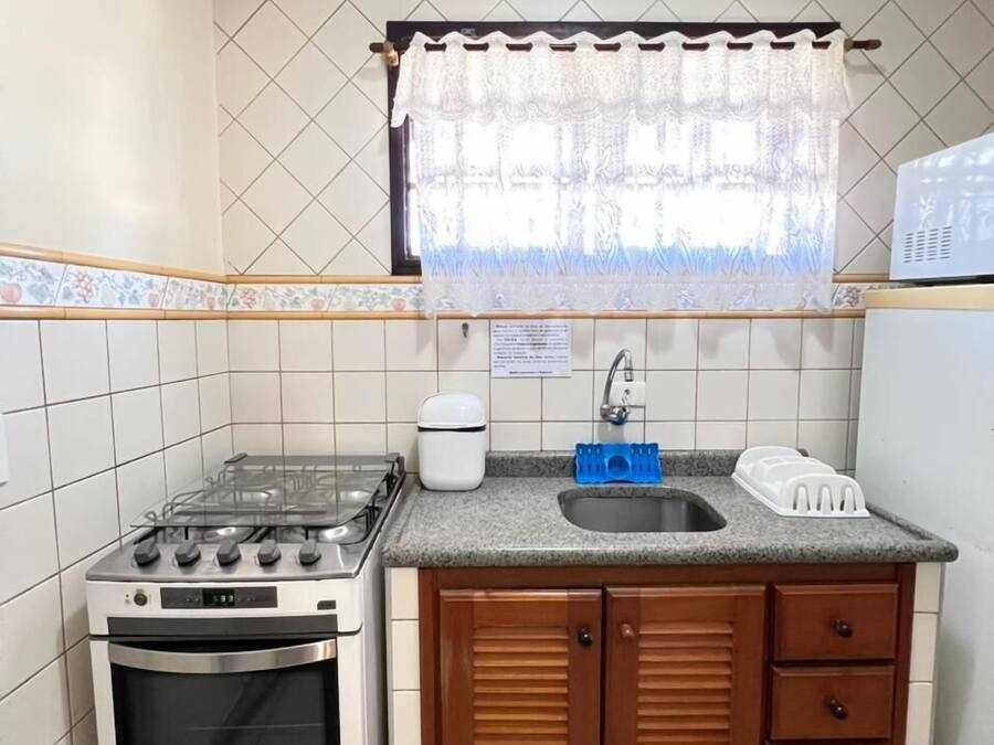 Cozinha compacta com fogão a gás, forno, pia e armários de madeira.